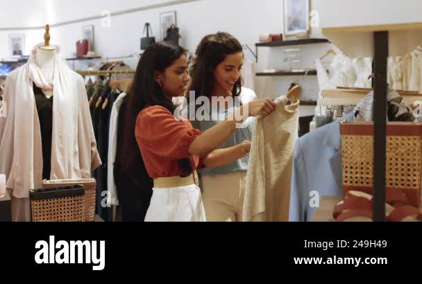 Two young women browsing through clothing racks, examining cream ...