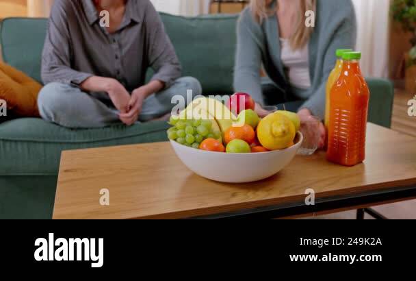 Two joyful women enjoy a healthy snack of fresh fruits and juice while ...