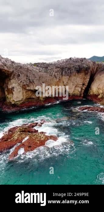 Raging blue sea water splashes by the rocks. Unapproachable mountains ...