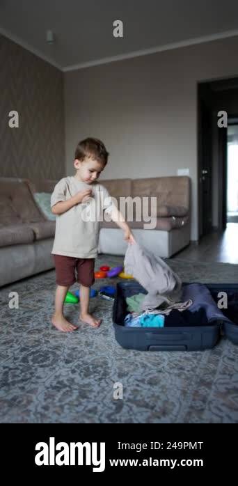 Little Caucasian toddler packing a big suitcase. Kid puts some clothes ...
