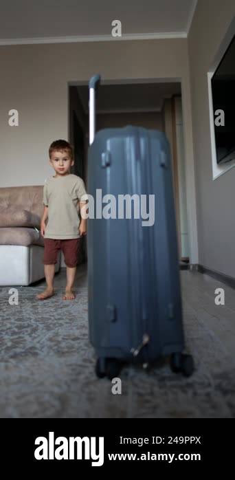 Toddler kid stands at the big grey suitcase in the room. Little boy ...