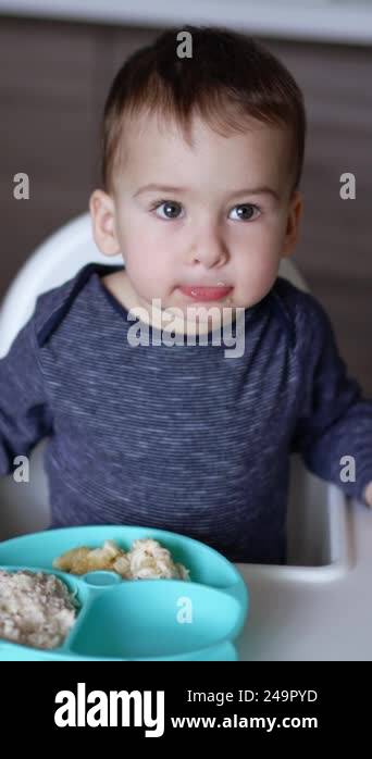 Baby boy sits in a high chair holding it on two sides. Little kid is ...