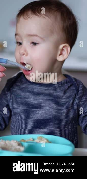 Little Caucasian toddler holding a fork in hand while mom feeds him ...