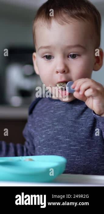 Lovely Caucasian child eating from fork himself. Baby boy chewing food ...