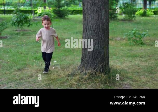 Cute Caucasian baby boy runs around the tree in the park. Little kid ...