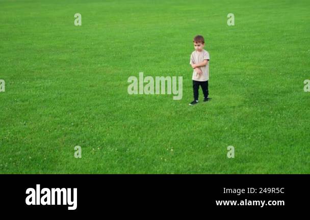 Little kid stands on the green lawn. Toddler boy plays cheerfully with ...