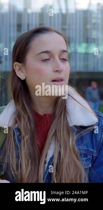 Vertical HD video of young caucasian student girl leaving university campus after classes ...