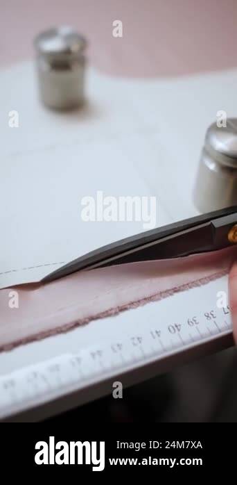 A precise close-up of hands cutting soft pink fabric with scissors on a ...