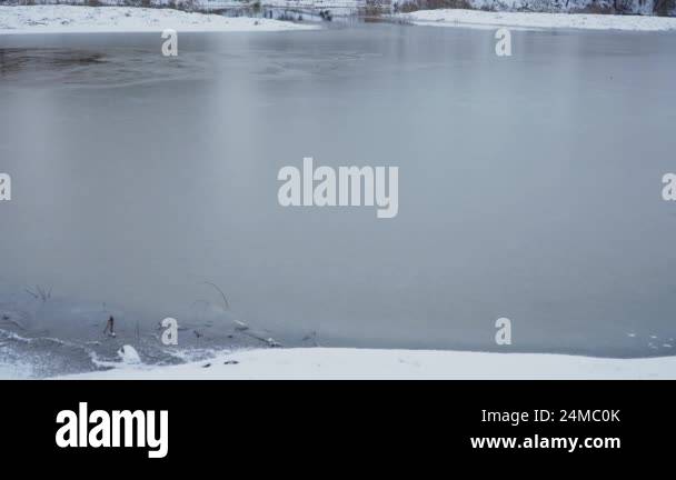 A serene winter scene featuring a nearly frozen lake with a smooth ice ...