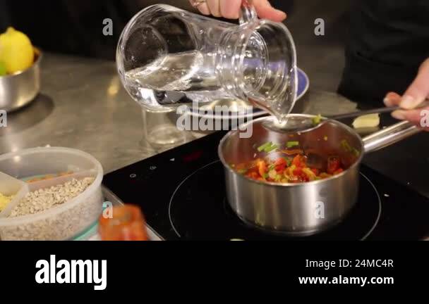 Water jug, Tomato pouring, Induction sauce. Water is being poured from jug into pan vegetable ...