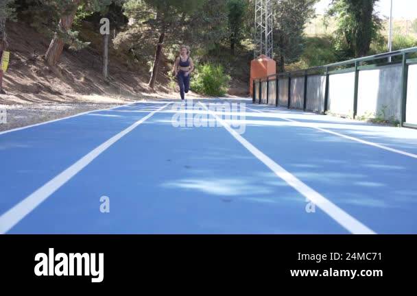 In a tranquil park, a determined young woman is running on a blue track ...