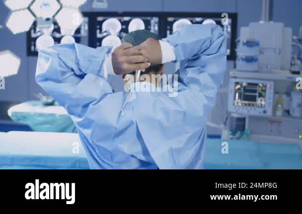 Male surgeon tying his surgical cap at the back of his neck in ...