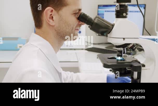 Man in lab coat and latex gloves using microscope to examine sample ...