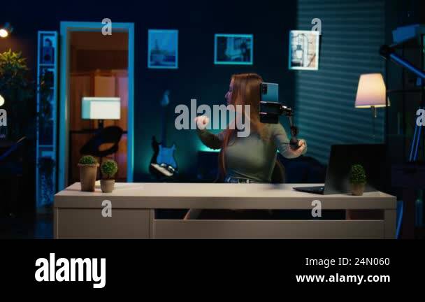 Girl in neon lit apartment using phone on selfie stick to capture ...