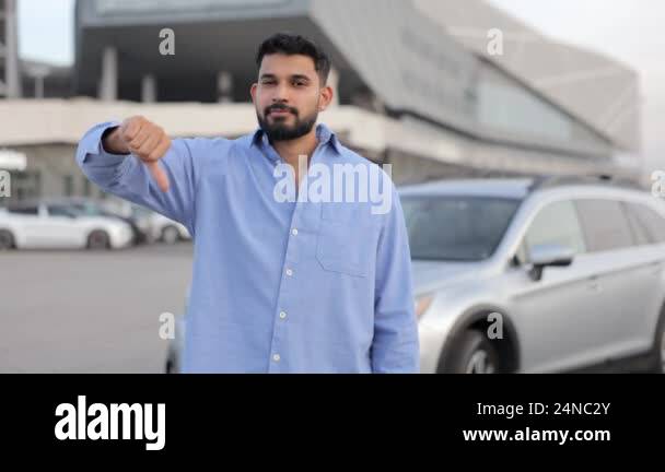 Unhappy male driver showing thumbs down to camera, while standing in ...
