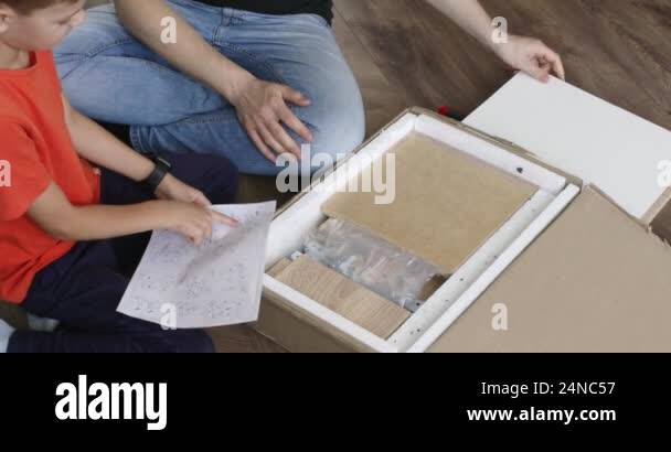 Preschooler and father sit on floor unpacking cardboard box. Young boy ...