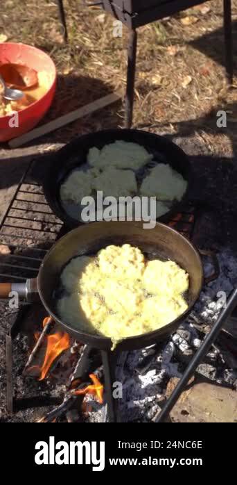 Fry potato pancakes on open fire in a frying pan. Camping dinner ...