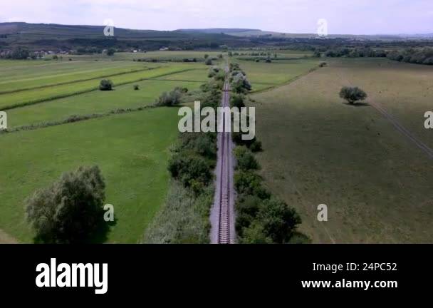 Train tracks stretching across a picturesque countryside, surrounded by lush green fields and ...