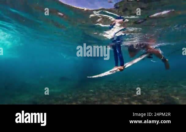 Surfer wearing a blue rashguard executes a duck dive, showcasing the ...