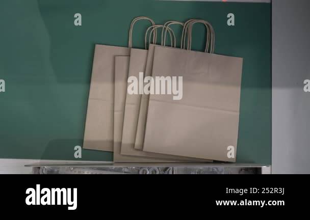 Mechanism folds finished paper shopping bags onto moving conveyor ...