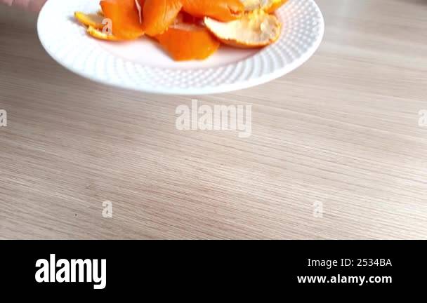 A woman puts a plate with a mandarin peel on the table. The benefits of ...