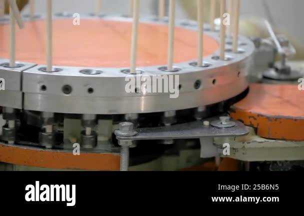 A machine processes wooden dowels, arranging them vertically in a ...