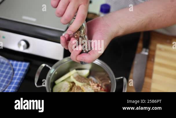 Man adds ground hot pepper from hand mill into pot with sliced zucchini ...