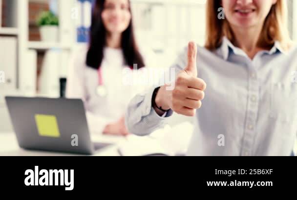 In a bright medical office, a satisfied patient gives a thumbs up ...