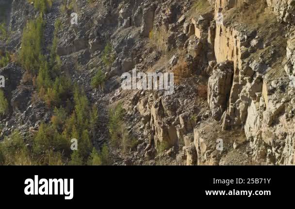 Rocky cliff with rough textures, golden sunlight, and sparse vegetation ...
