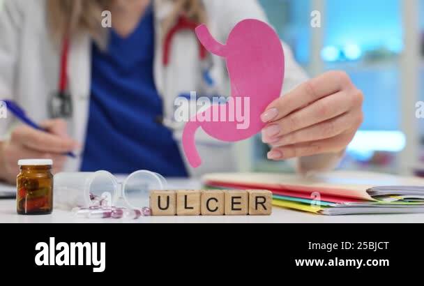 Word Ulcer on cubes and doctor showing paper stomach at table. Woman ...