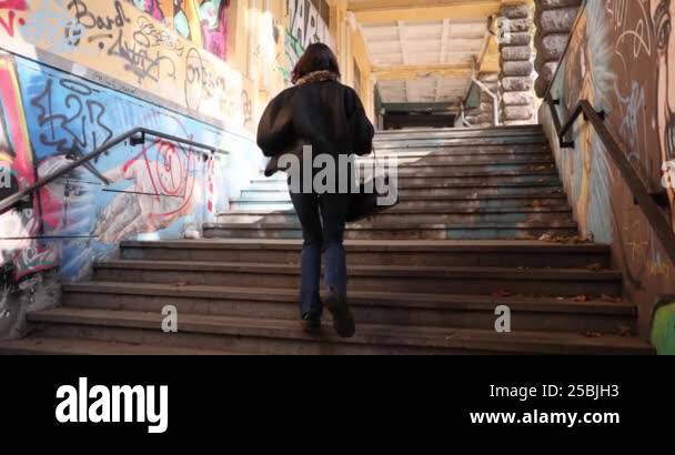 Young woman in outwear runs up street stairs with walls covered in ...