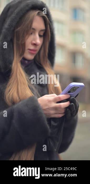 Stylish woman in luxurious fur coat and leather gloves using mobile ...
