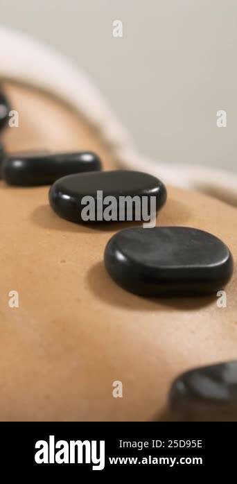 Masseuse placing hot stones on a clients back while the client relaxes ...