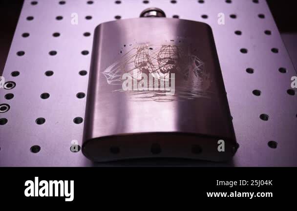 A close-up view of a metal flask featuring an engraved ship design ...