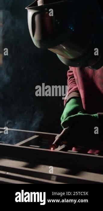 Skilled blacksmith in protective mask welds steel frame in plant ...