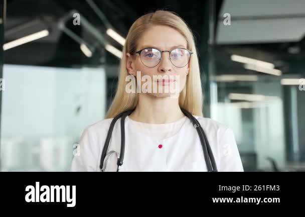 Portrait of confident female doctor in white coat with glasses looking ...