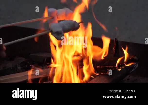 Hands roasting marshmallows on two sticks over a warm grill fire on a ...