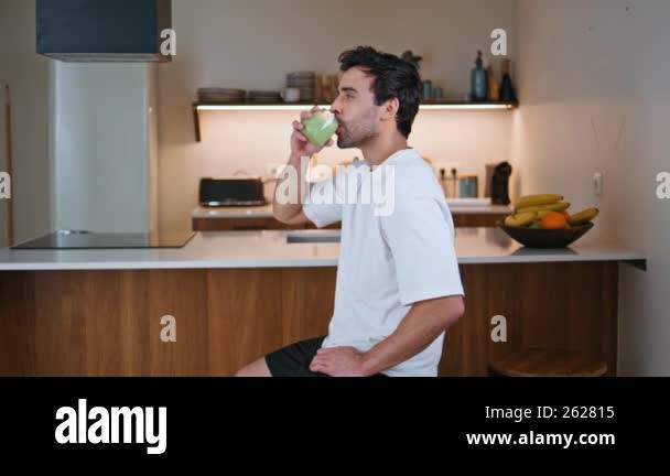 Guy enjoy vitamin smoothie sitting modern kitchen after morning workout ...