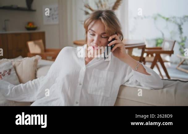Beautiful lady calling mobile phone relaxing at apartment sofa in white ...