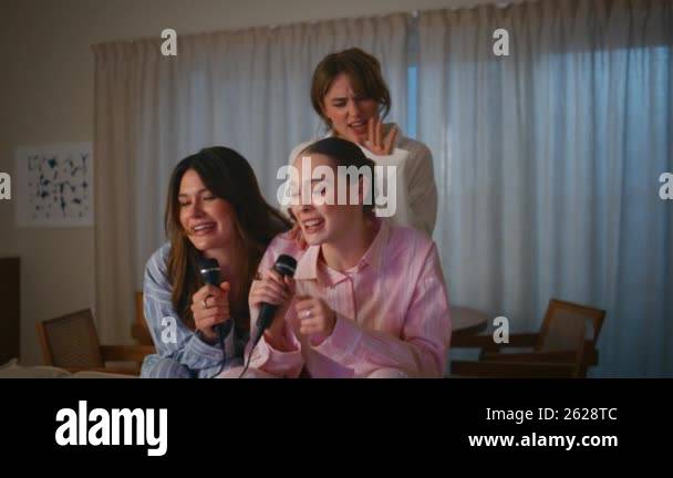 Happy women singing karaoke in pajamas at friendly sleepover. Joyful ...