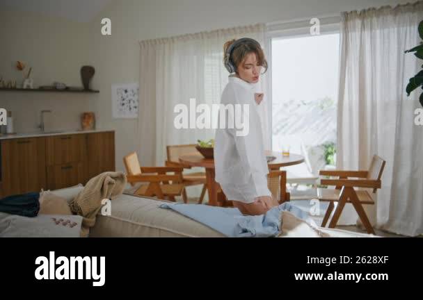 Homely woman listening music in wireless earphones tidying up modern ...