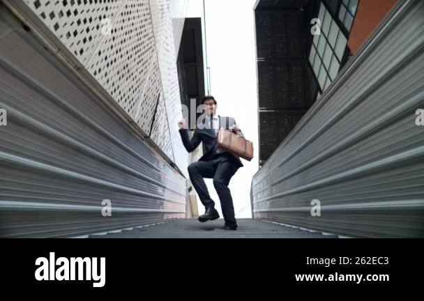 Low angle view of young smiling business man dance between building at ...