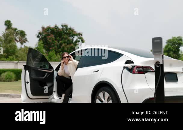 Young woman put EV charger to recharge electric cars battery from charging station. Alternative ...
