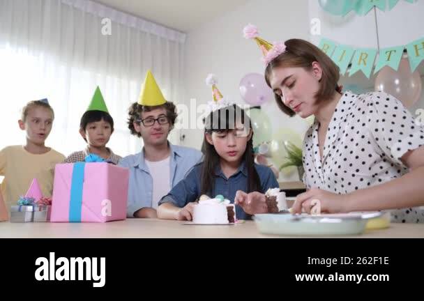 Caucasian mother cutting cake while family congratulate in girls ...