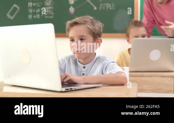 Caucasian boy working at laptop while diverse children programing software system. Teacher and ...