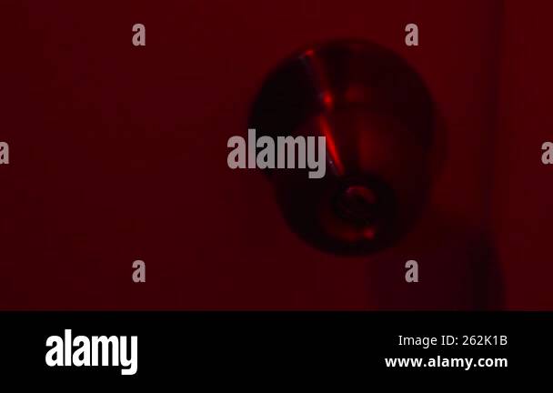 The door handle twists in the flickering red light, casting elongated ...