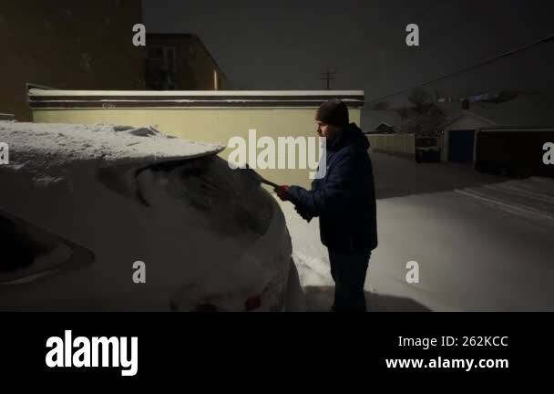 In the early hours of a cold, dark morning, a man clears snow from his ...