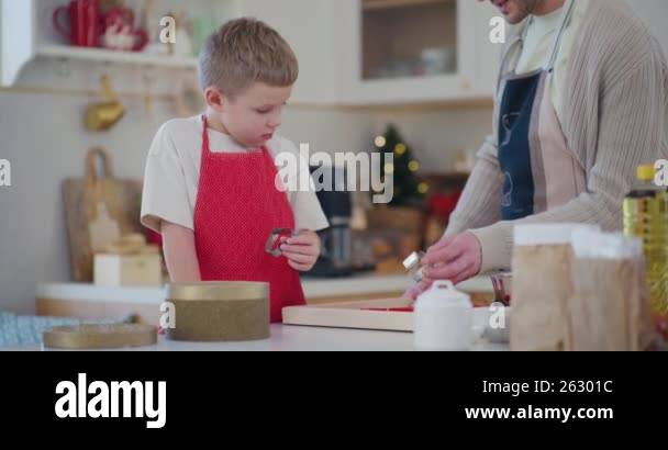 In the kitchen, a dad and his son prepare cookie cutters together while ...
