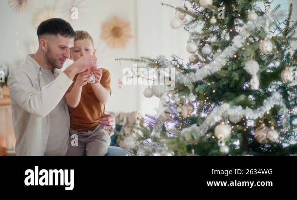 A close-up of a young boy and his father carefully placing baubles on the Christmas tree Stock ...