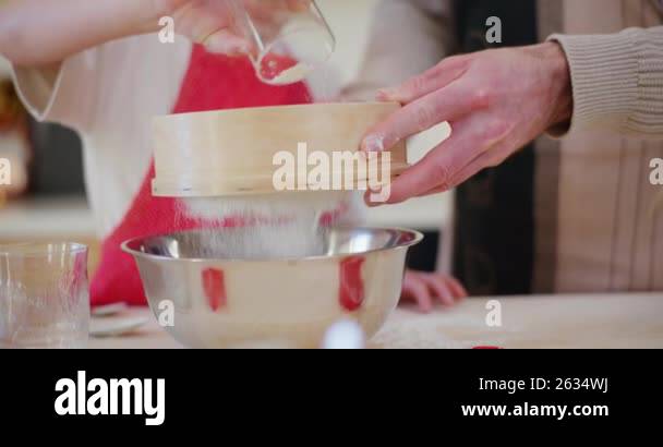 A detailed close-up shows flour being sifted through a sieve during the ...